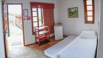 Quarto com uma cama, uma pequena escrivaninha, uma cadeira, uma janela e uma porta para o exterior.