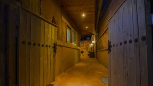 Um corredor com paredes e portas de madeira, que dá para um quarto com cama e janela.