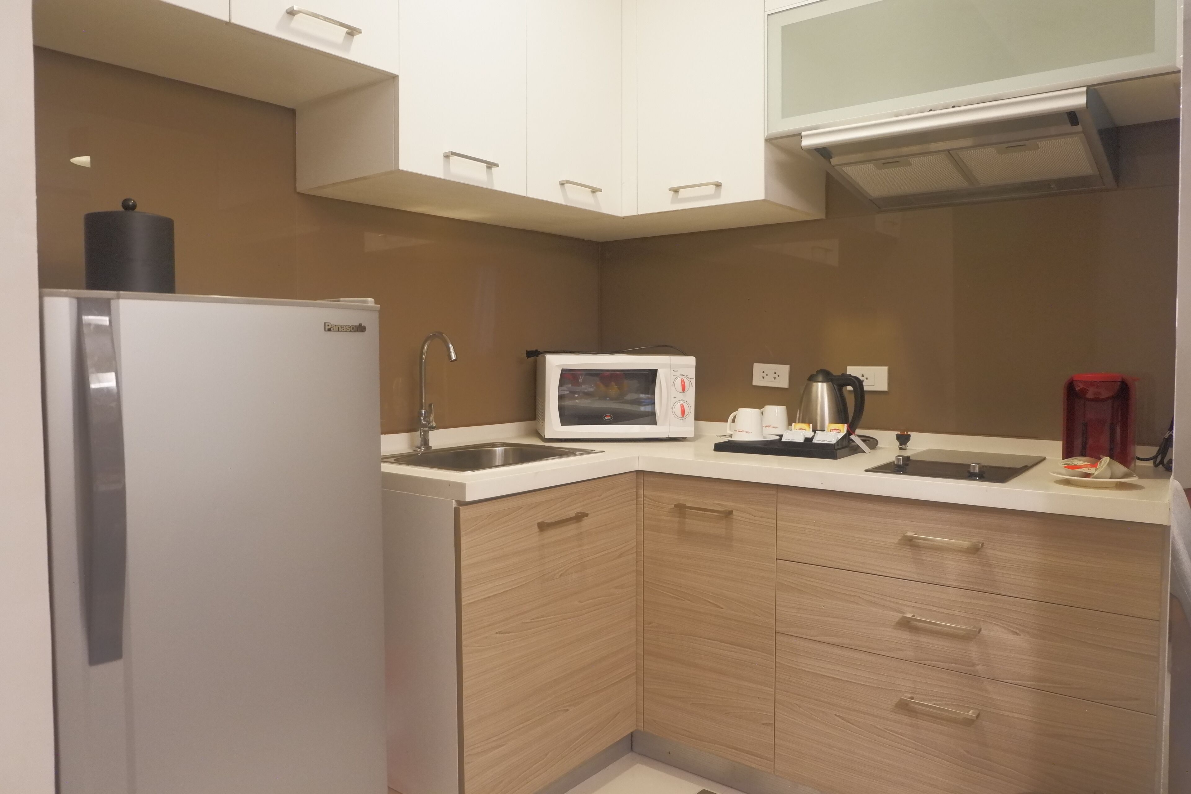 Cozinha compacta com geladeira, micro-ondas, pia e armários de madeira.