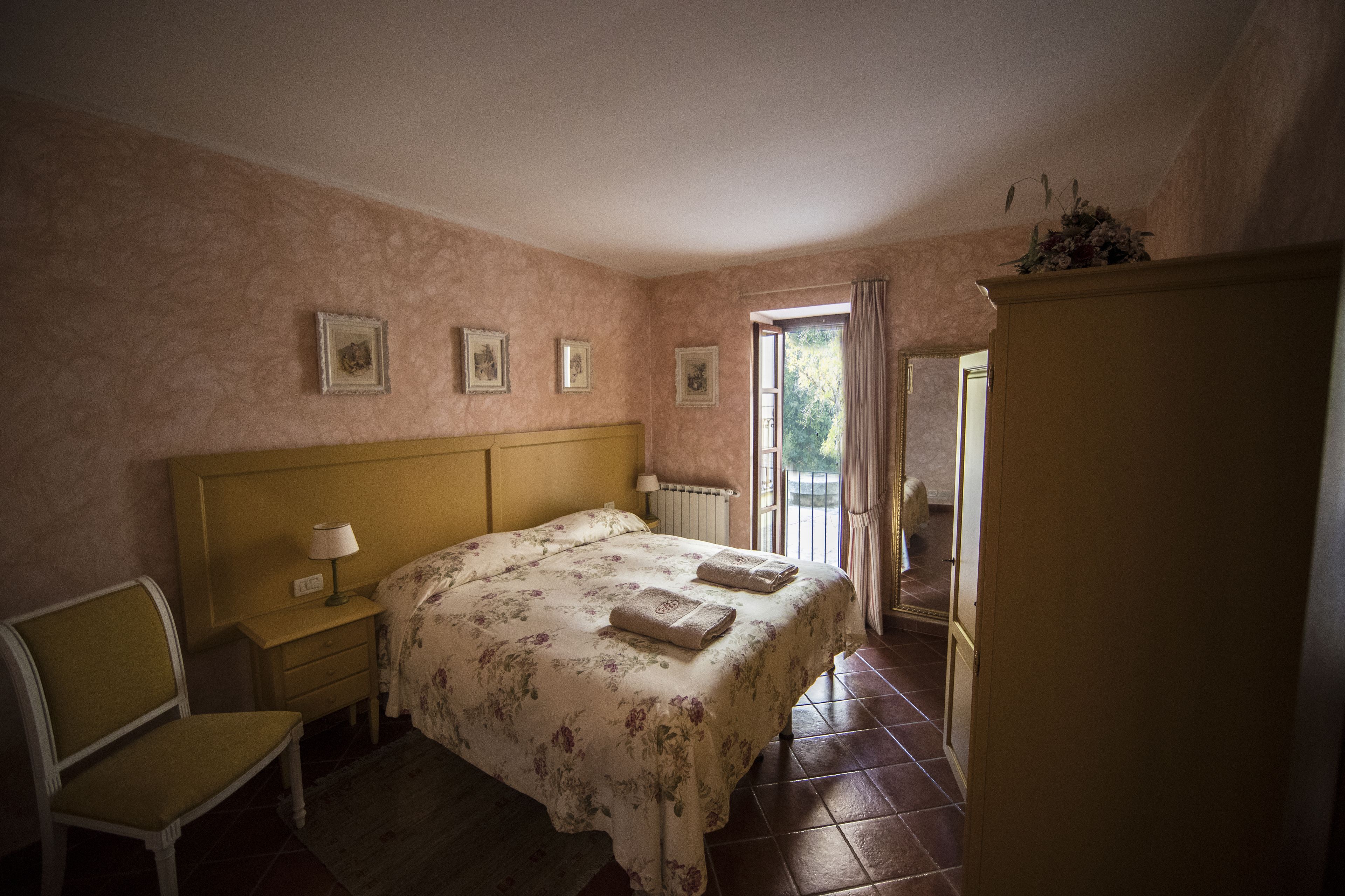 Quarto com cama, cadeira, mesa de cabeceira, cômoda e janela com cortinas.