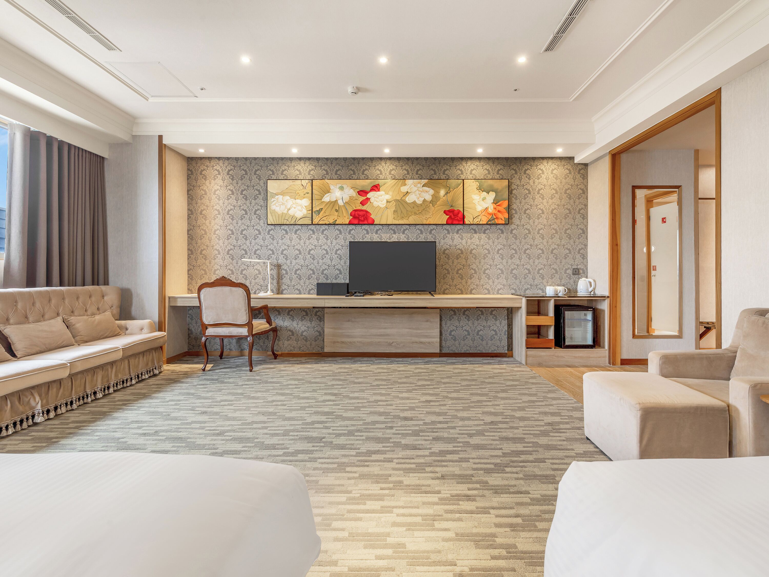 Quarto de hotel com sofá, escrivaninha, cadeira, televisão e um objeto decorativo na parede.