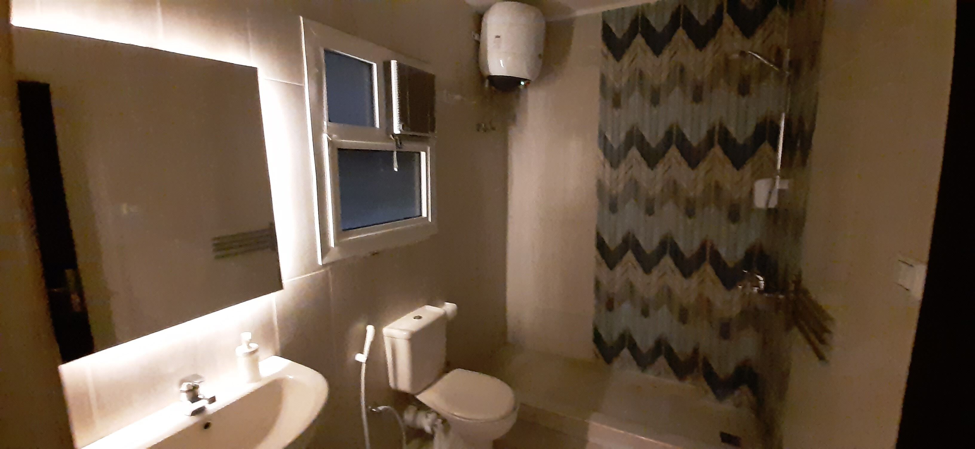 Casa de banho com lavatório branco, sanita e chuveiro com azulejos estampados.