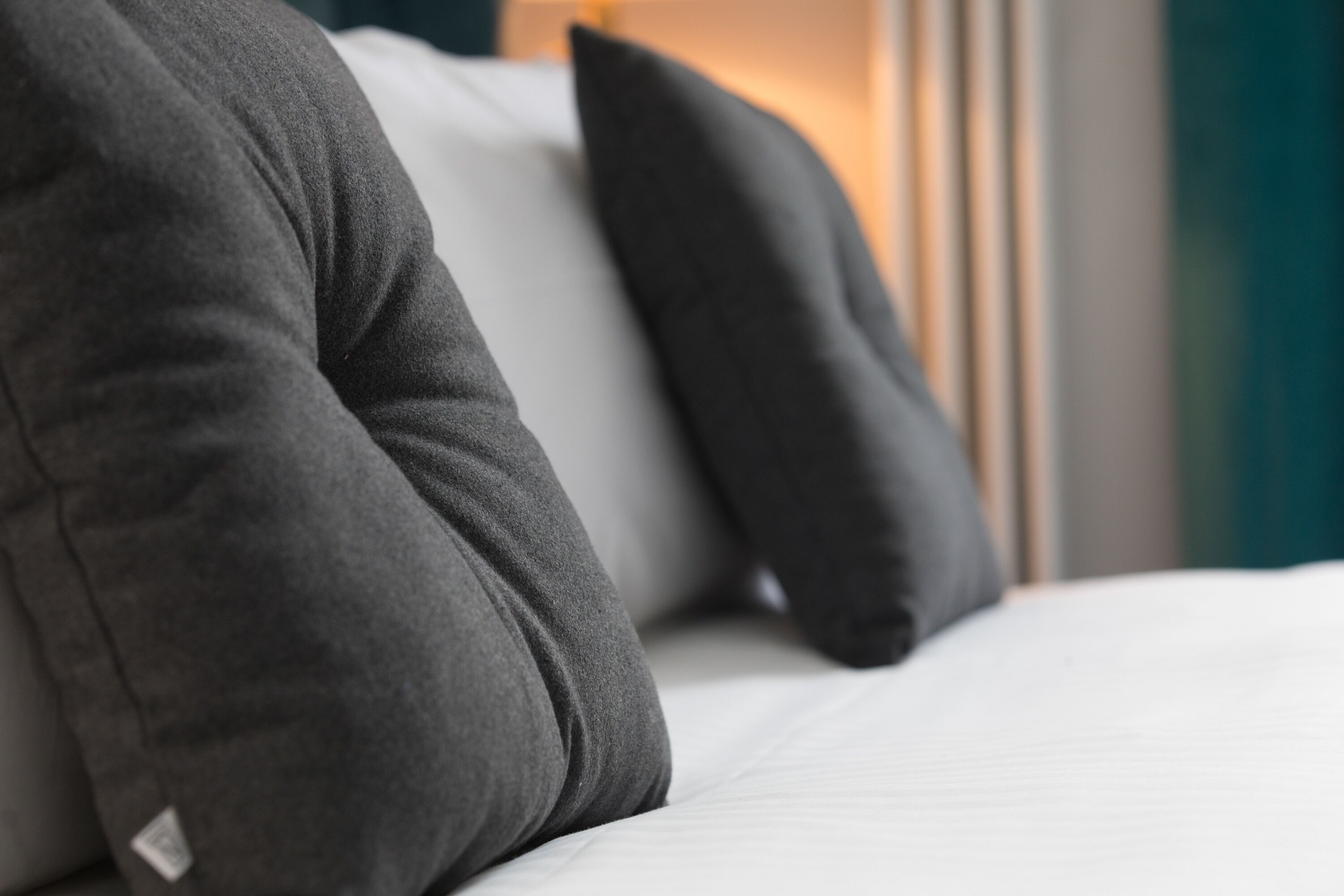 Um close-up de uma cama com roupa de cama cinza e branca, travesseiros e uma etiqueta visível em um dos travesseiros.