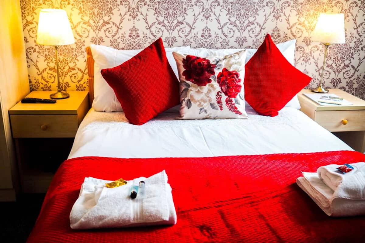 Quarto de hotel com cama bem arrumada, roupa de cama vermelha e branca e travesseiro floral.
