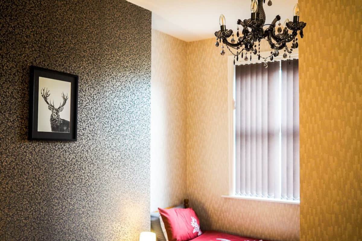 Quarto com cama, lustre, janela com cortinas e quadro na parede.