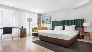 Quarto de hotel moderno com uma cama grande, uma escrivaninha, uma cadeira, um abajur e um quadro na parede.