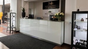 Uma mesa de recepção com tampo de vidro, uma placa acima e uma vitrine com objetos.