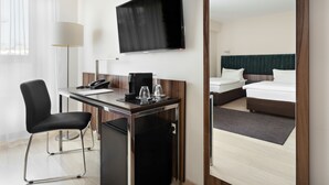 Quarto de hotel com escrivaninha, cadeira, televisão, cama e um pequeno frigorífico.