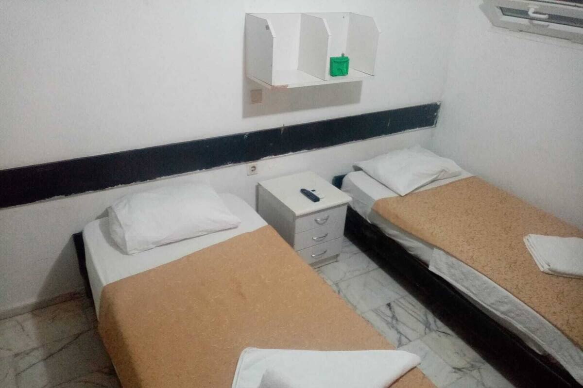 Quarto pequeno e limpo com duas camas de solteiro, uma mesa de cabeceira com telefone e um prateleira com uma garrafa verde.