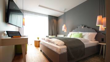 Quarto de hotel moderno com cama, secretária com um laptop, televisão de ecrã plano e iluminação ambiente.