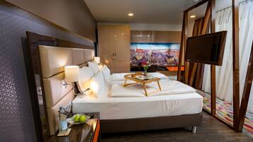 Quarto de hotel com cama, mesa de cabeceira, luminária, televisão e uma pintura de paisagem urbana.