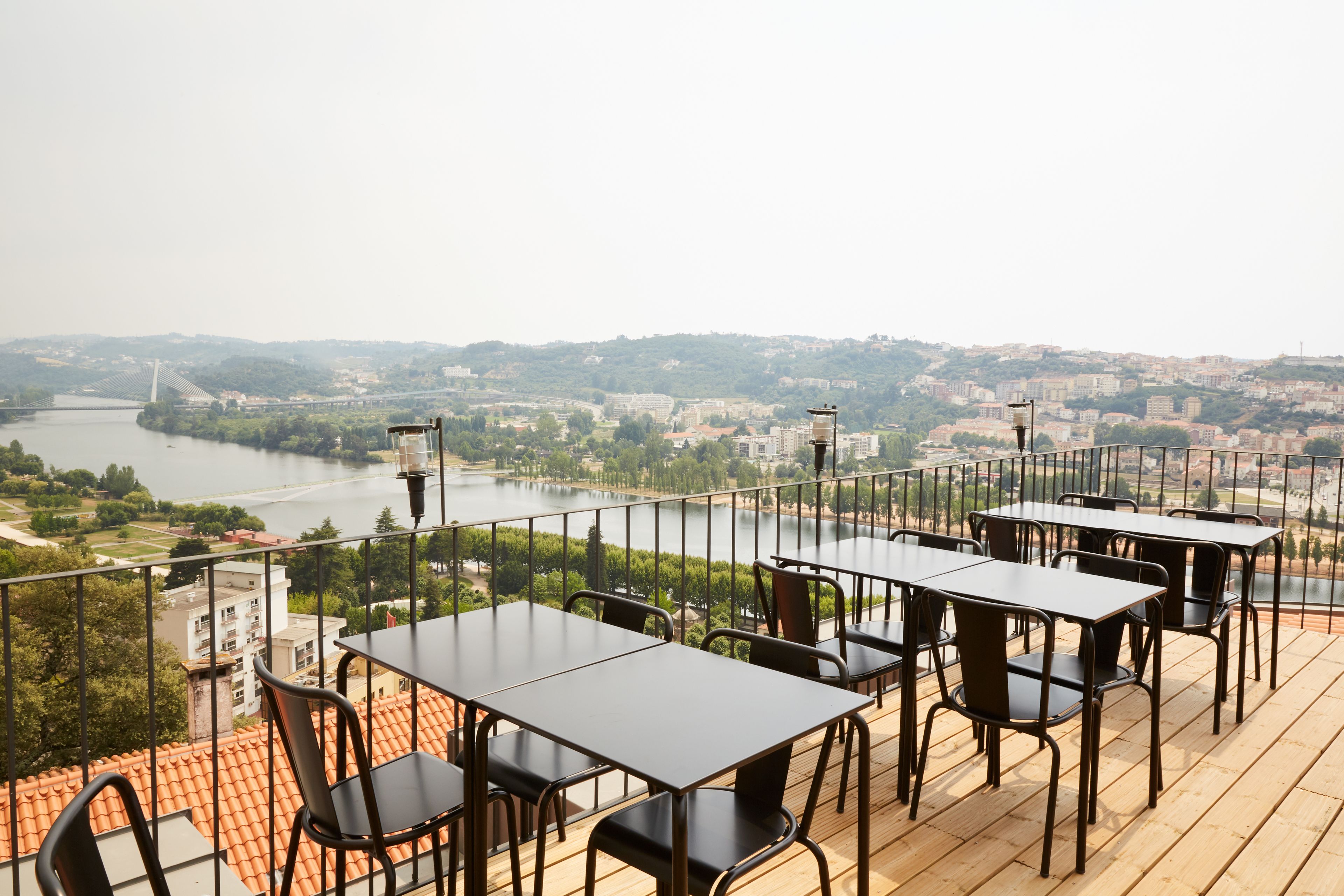 Terraço com mesas e cadeiras com vista para um rio e paisagem urbana.