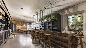 Uma área de bar moderna com banquetas de madeira, balcão e prateleiras com copos e garrafas.