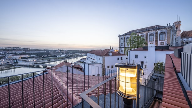 Terraço com telhas vermelhas, um lampião e vista para um rio e edifícios ao fundo.