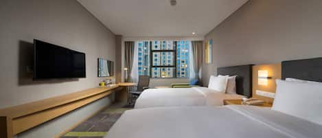 Quarto de hotel com duas camas, uma escrivaninha, televisão de tela plana, janela com vista para a cidade e abajur.