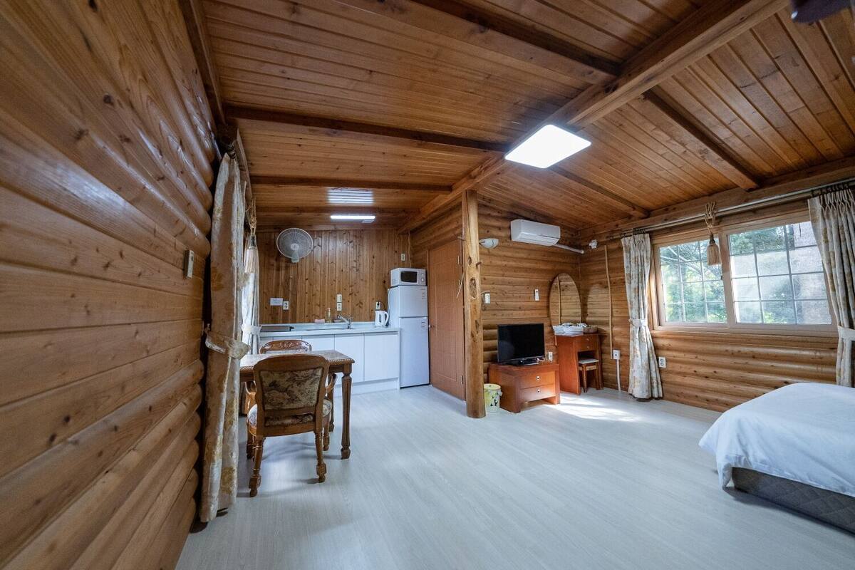 Interior de uma cabana de madeira com mesa de jantar, cadeiras, cozinha, televisão e cama.