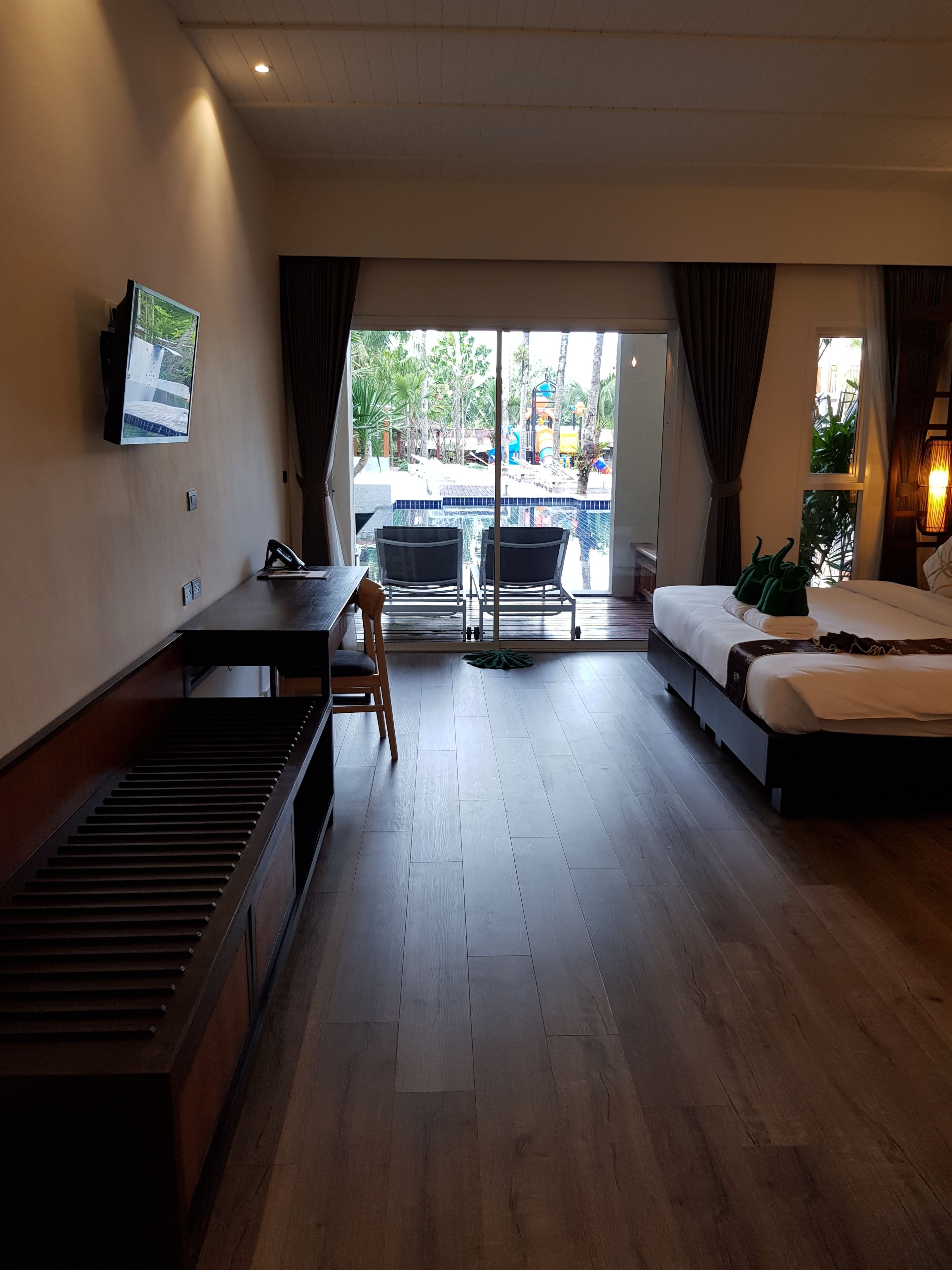 Quarto de hotel com piano, cama, escrivaninha e vista para a piscina e área externa.
