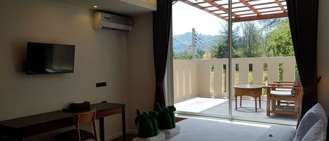 Quarto de hotel com cama, escrivaninha, cadeira, televisão, ar condicionado e varanda com vista para o exterior.