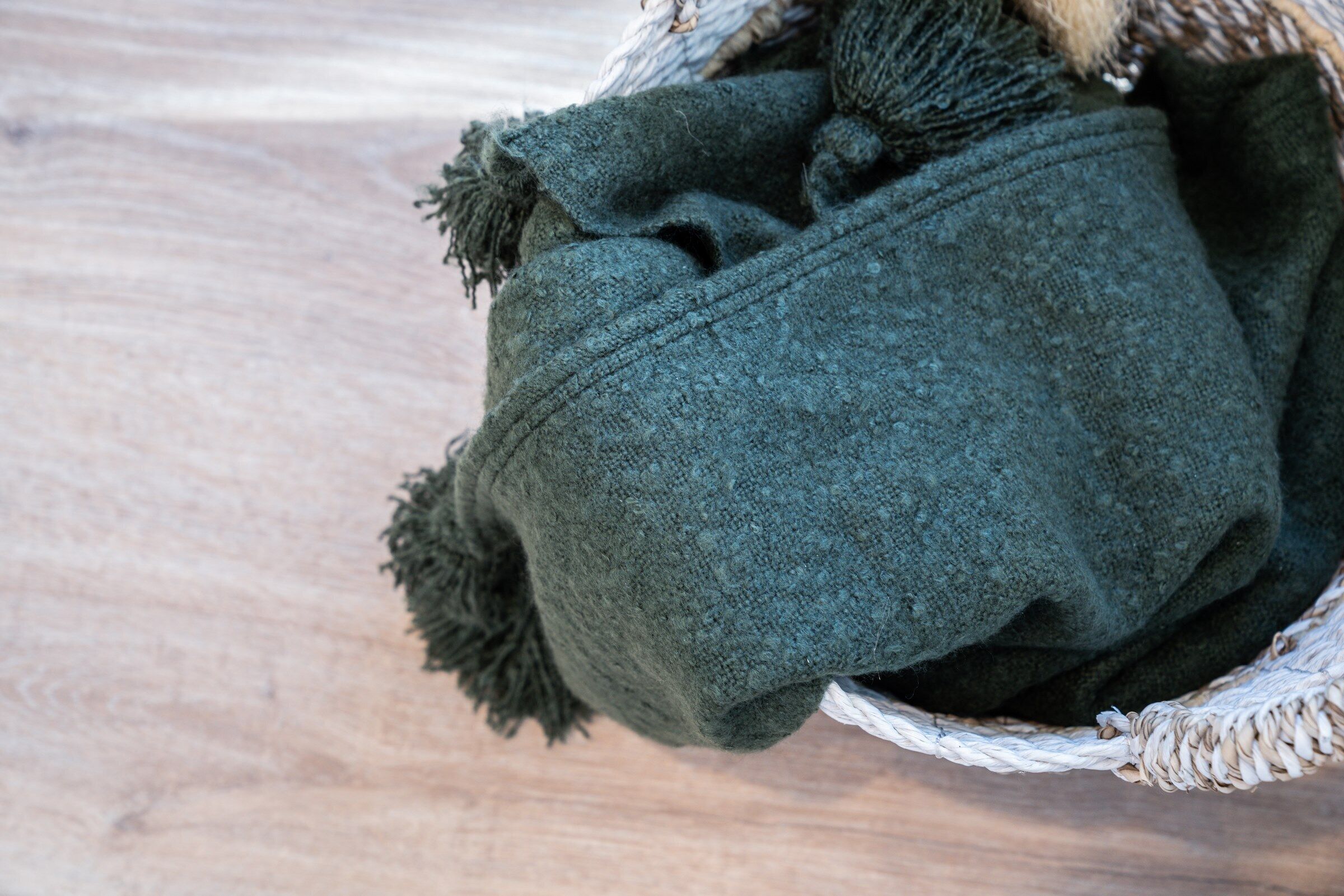Um close-up de um gorro verde de malha com um pompom, dentro de uma cesta trançada.