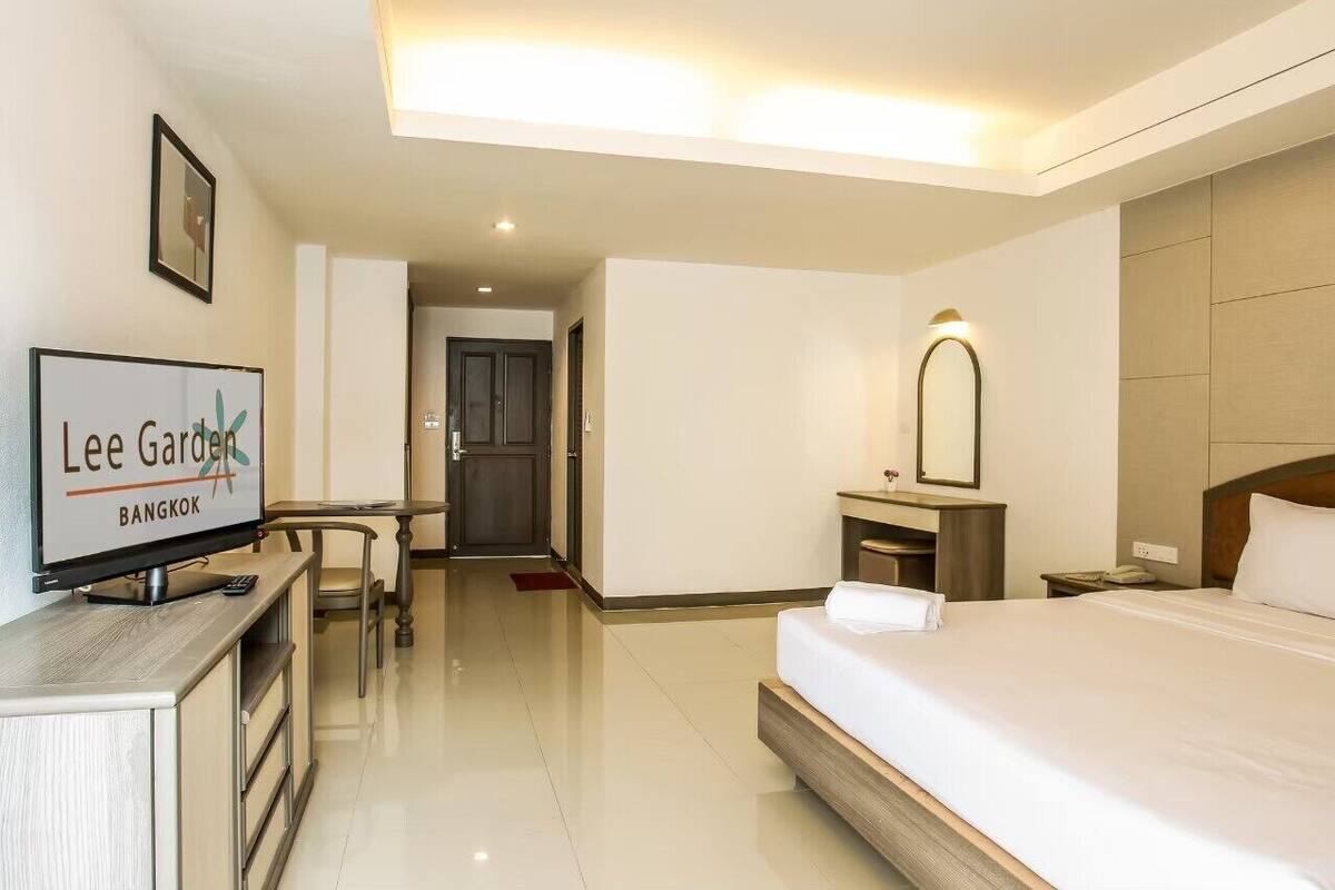 Quarto de hotel com cama, escrivaninha com televisão, espelho e porta para o banheiro.