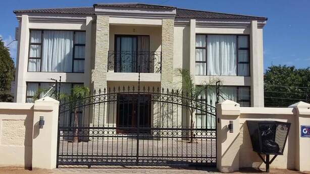 Uma casa de dois andares com portão fechado, varanda e um pequeno jardim.