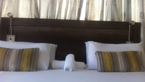 Cama bem arrumada com lençóis brancos, duas almofadas listradas e uma toalha branca enrolada.