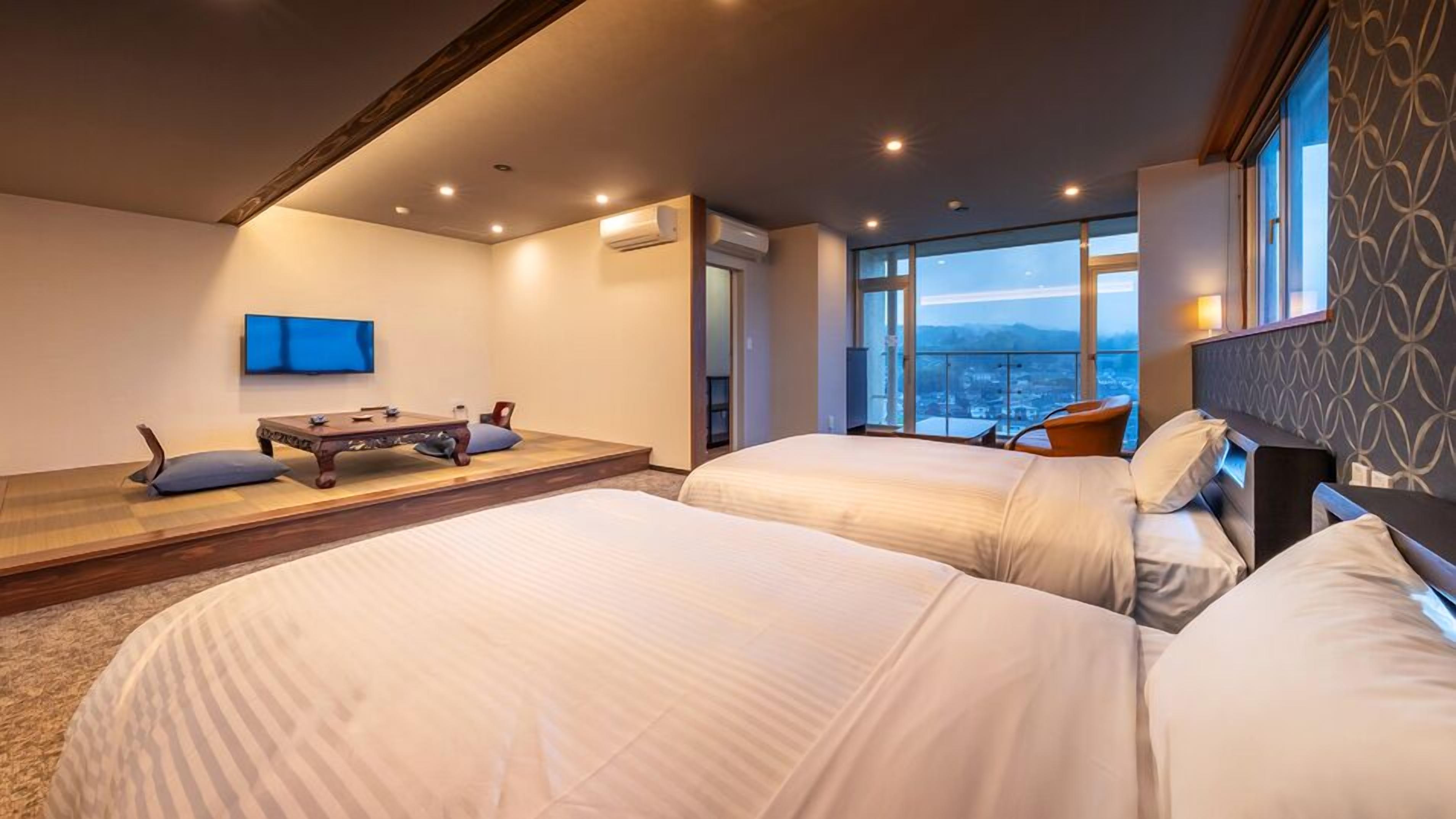 Quarto de hotel com duas camas, uma televisão de tela plana, uma pequena mesa com um jogo de tabuleiro e vista para a cidade.