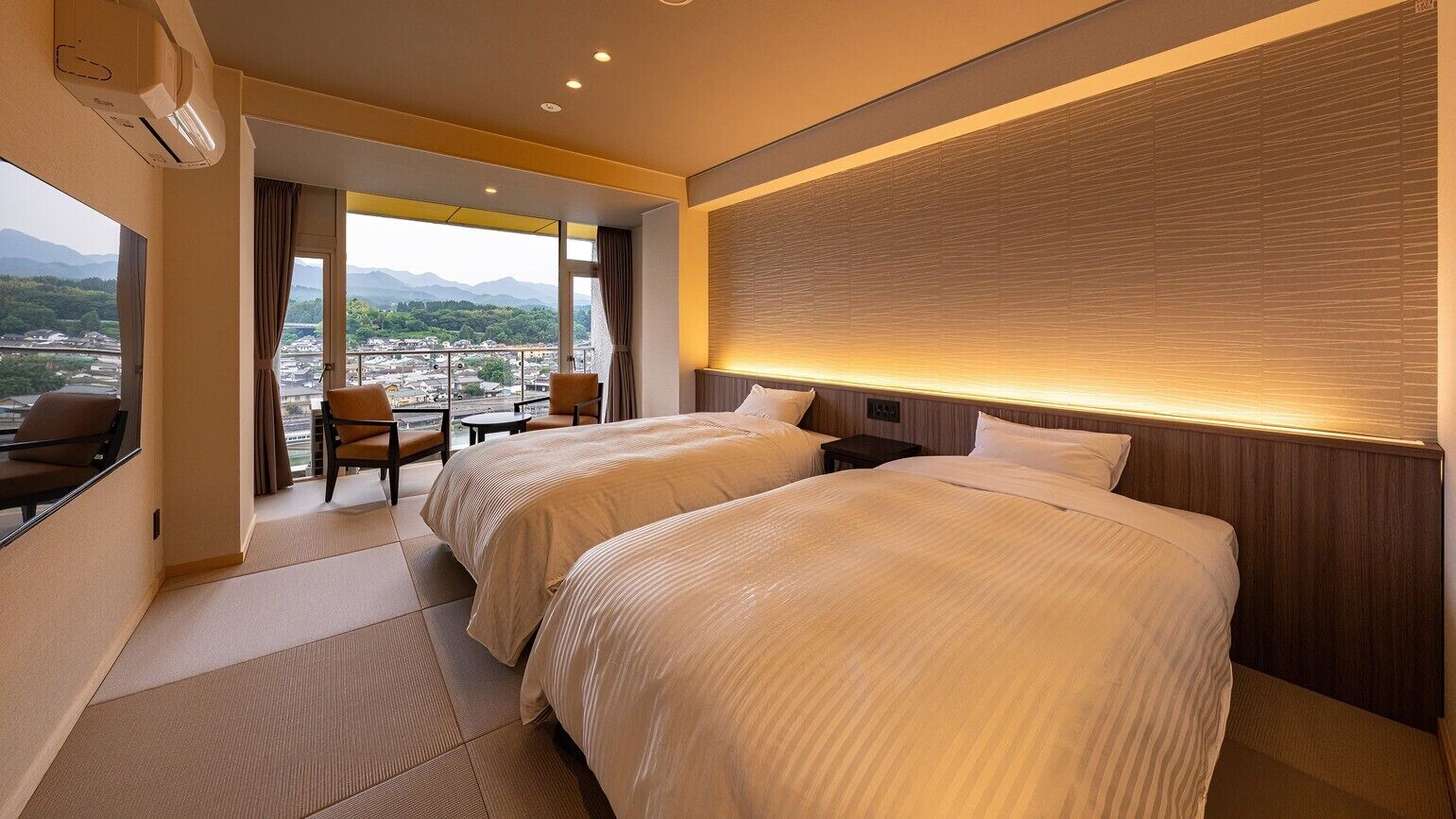Quarto de hotel com duas camas, vista para a cidade e varanda.