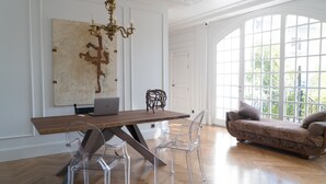 Uma área de jantar moderna com mesa de madeira, cadeiras transparentes, um laptop e um objeto decorativo na parede.