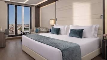 Quarto de hotel moderno com uma cama grande, um sofá, uma escrivaninha e vista para a cidade.