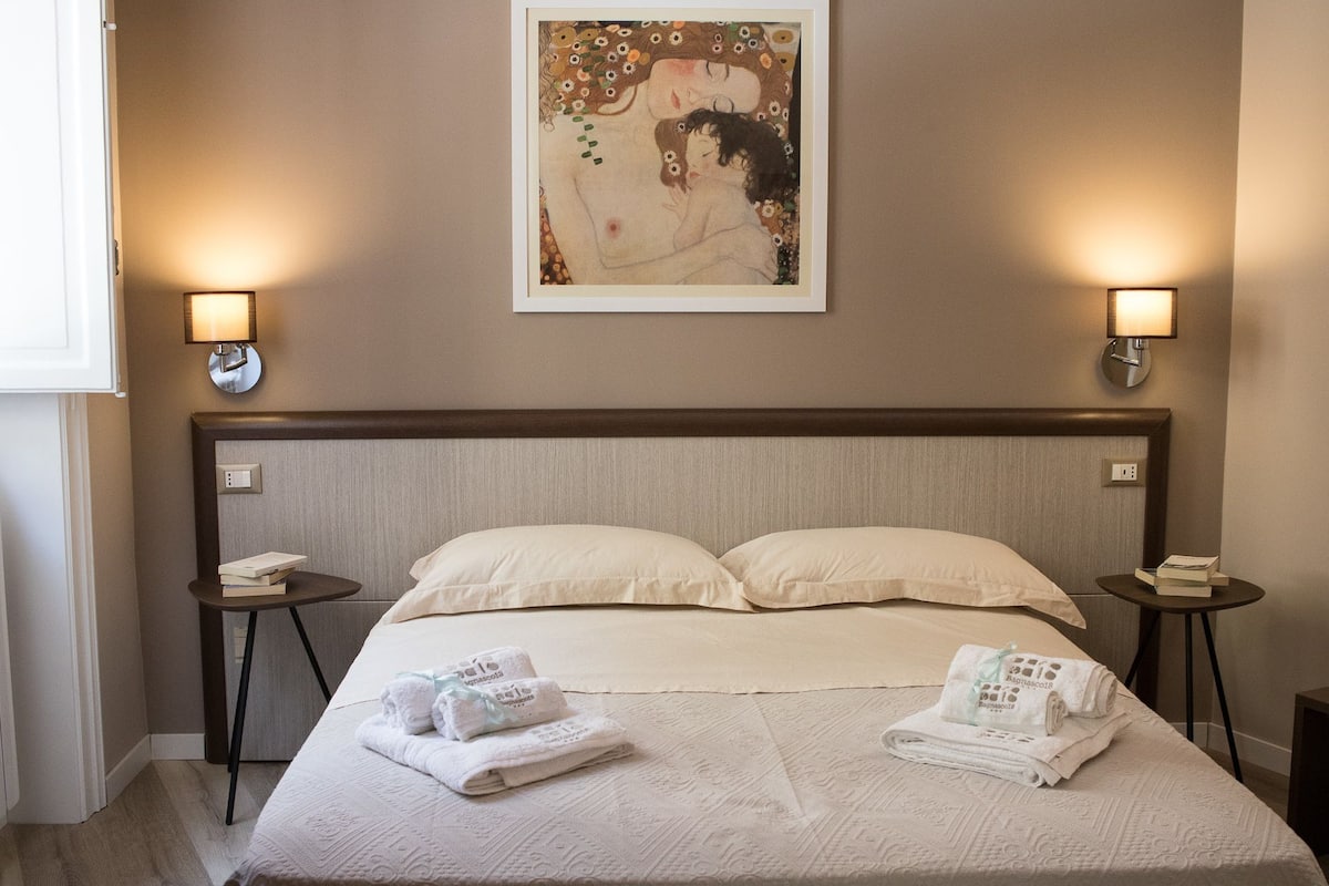 Quarto de hotel com cama, duas mesas de cabeceira e um quadro na parede.