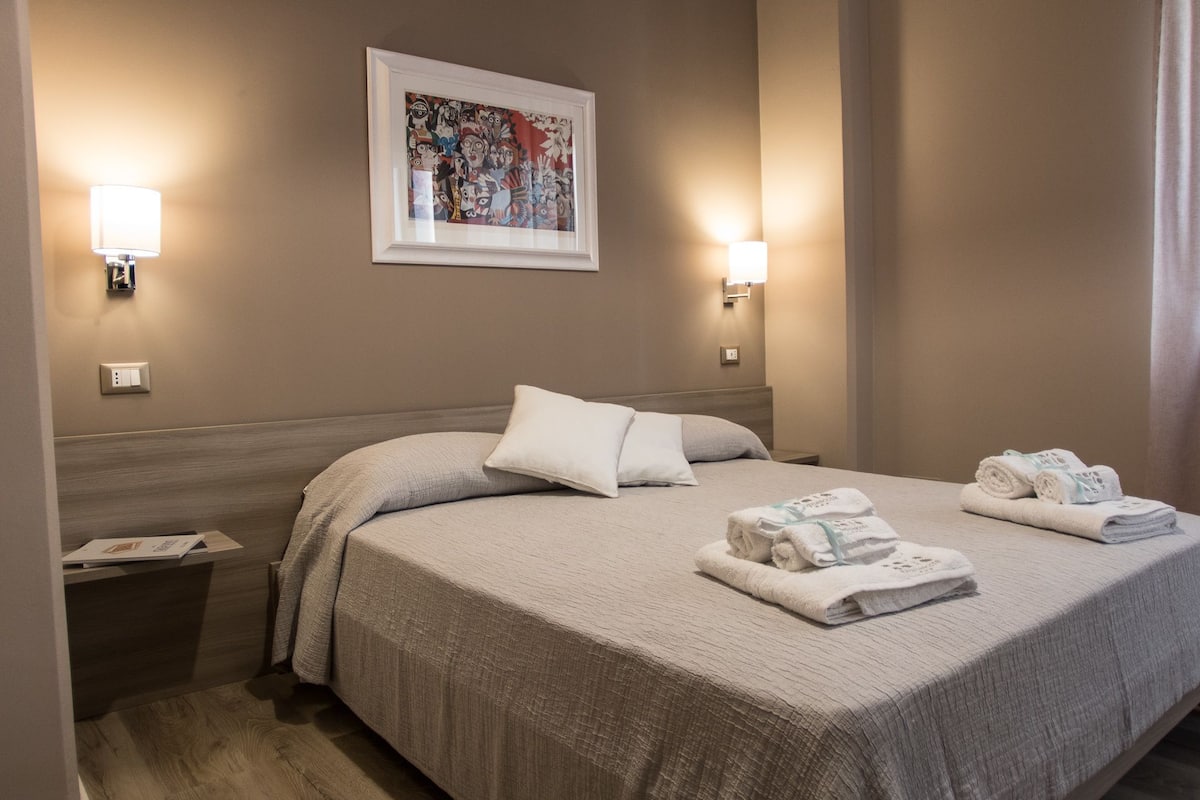 Quarto de hotel com uma cama, duas luminárias de cabeceira, uma obra de arte emoldurada e toalhas sobre a cama.