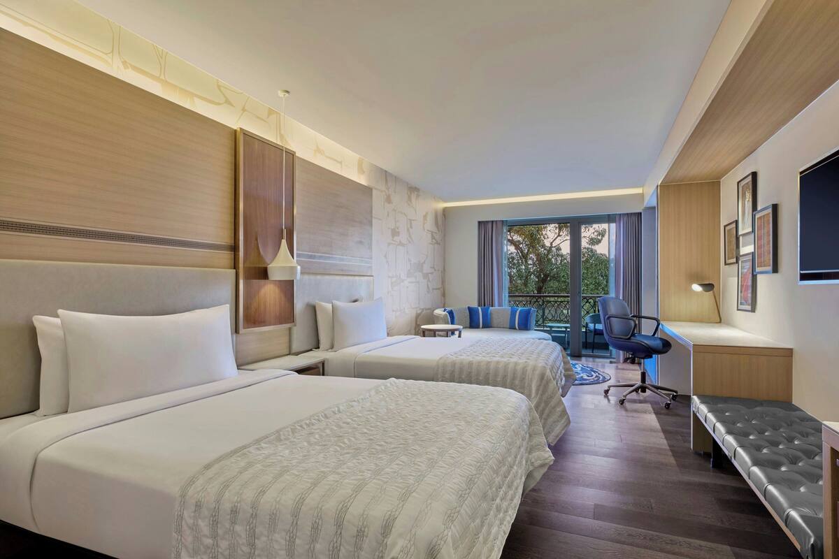 Quarto de hotel com duas camas, uma escrivaninha, uma cadeira e uma televisão.