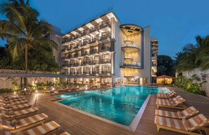 Um hotel com piscina, espreguiçadeiras e fachada bem iluminada.