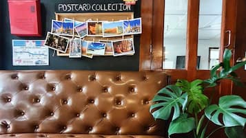 Um sofá de couro marrom num quarto com um quadro negro exibindo informações do aeroporto e uma coleção de postais.