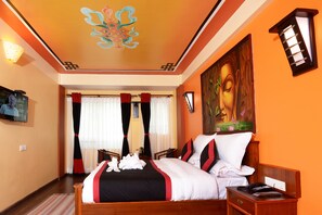 Quarto de hotel com cama, mesa de cabeceira, um quadro e televisão na parede.