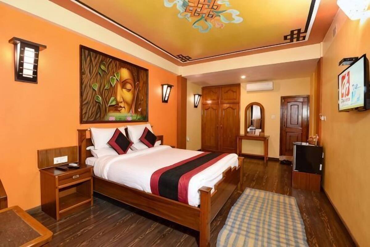 Quarto de hotel com cama de madeira, uma secretária, uma cadeira e um quadro grande na parede.