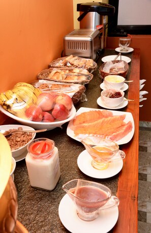 Uma mesa de buffet com diversos alimentos, incluindo frutas, carnes e bebidas.