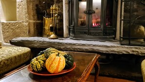 Uma sala de estar acolhedora com lareira de pedra, uma mesa de madeira com um prato de abóbora e um sofá estampado.