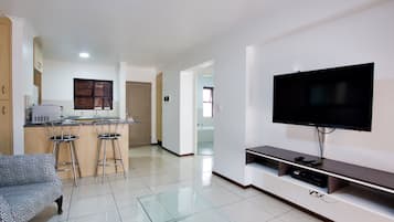 Uma sala de estar moderna com uma televisão de tela plana, uma mesa de centro de vidro e um sofá.
