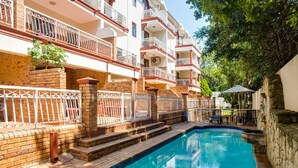 Piscina com deck de tijolos, cercada por um muro branco e uma parede de pedra.