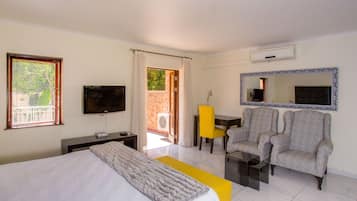 Quarto de hotel com cama, escrivaninha com cadeira, televisão e um espelho grande.