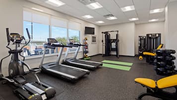 Uma academia com esteiras, um banco de musculação e diversos equipamentos de exercício.