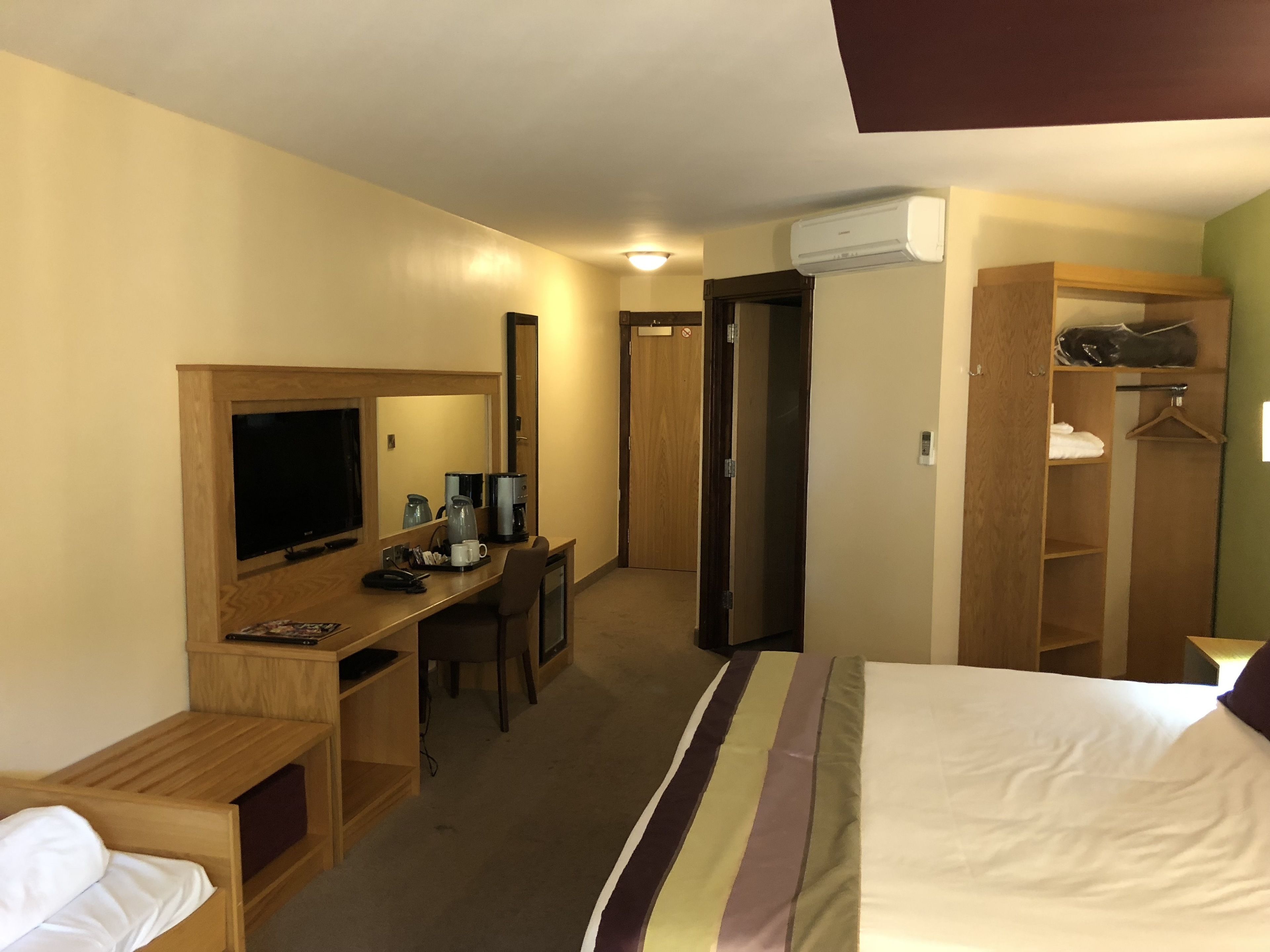 Quarto de hotel com cama, escrivaninha, televisão, máquina de café e guarda-roupa.