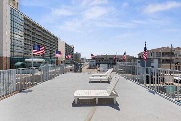 Terraço no telhado com cadeiras de lounge brancas, bandeiras americanas e vista de um prédio de hotel.