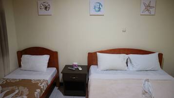 Quarto de hotel com duas camas de solteiro, uma mesinha de cabeceira com controle remoto e obras de arte nas paredes.