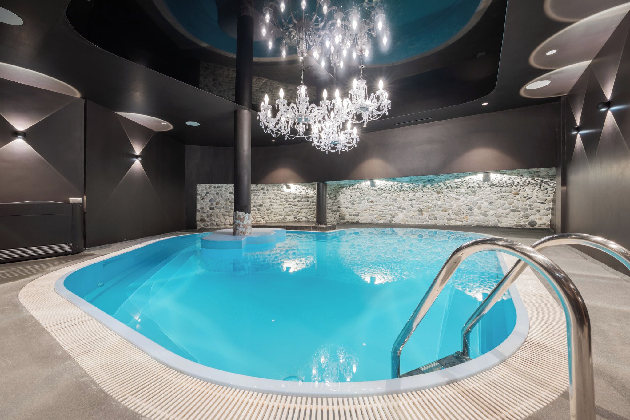 Piscina interna com design moderno, incluindo um candelabro e um painel de parede de pedra.