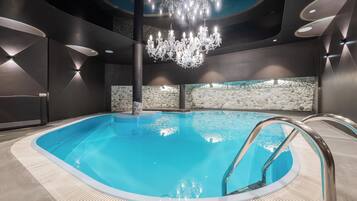 Piscina interna com design moderno, incluindo um candelabro e um painel de parede de pedra.