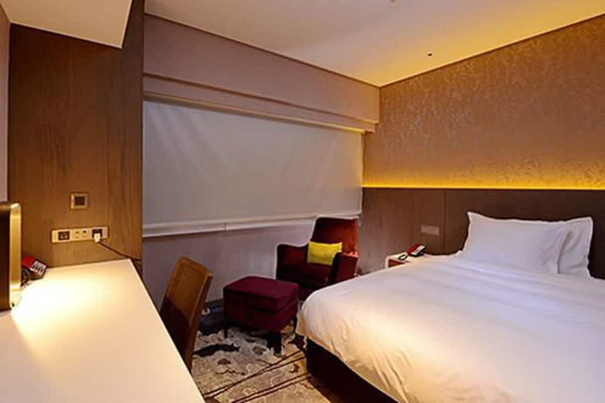 Quarto de hotel com uma cama grande, uma mesa, uma cadeira e uma janela com cortinas.