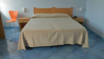 Quarto com cama, cadeira, mesa de cabeceira e telefone fixado na parede.